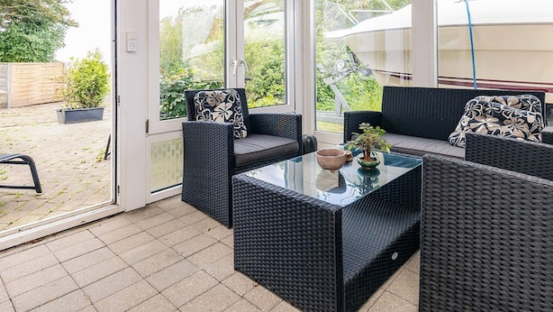 Pátio externo com mobiliário de vime e mesa de vidro, rodeado por grandes portas de correr.