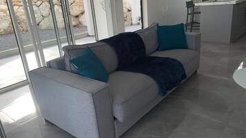 Uma sala de estar moderna com um sofá cinza, almofadas verde-água e uma porta de vidro que dá para o exterior.