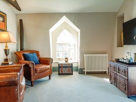 Uma sala de estar acolhedora com uma poltrona de couro marrom, uma mesinha lateral, um radiador e uma janela com vista para o exterior.