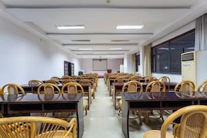 Sala de conferência com várias mesas e cadeiras, tela de projetor e uma janela grande.