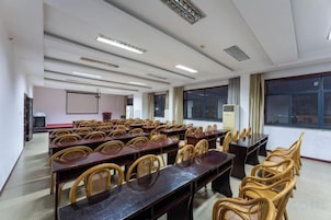 Uma sala de conferências com mesas e cadeiras compridas, uma tela de projetor e uma janela grande.