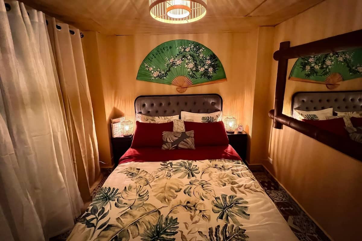Um quarto com uma cama grande, cabeceira, um ventilador pendurado e uma mesa de cabeceira com abajur.