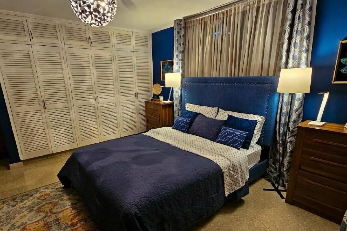 Quarto com cama, mesa de cabeceira, penteadeira, guarda-roupa e lustre.