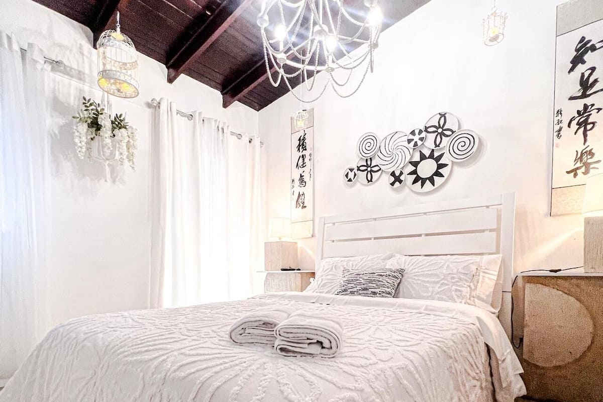 Quarto com cama grande, roupa de cama branca, um candelabro e arte decorativa na parede.