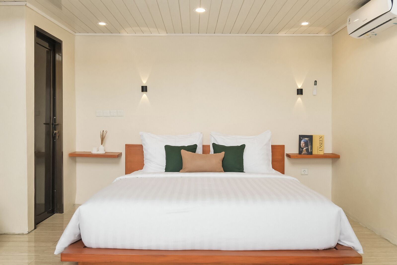 Quarto bem arrumado com uma cama grande, duas mesas de cabeceira e um ar condicionado fixado na parede.