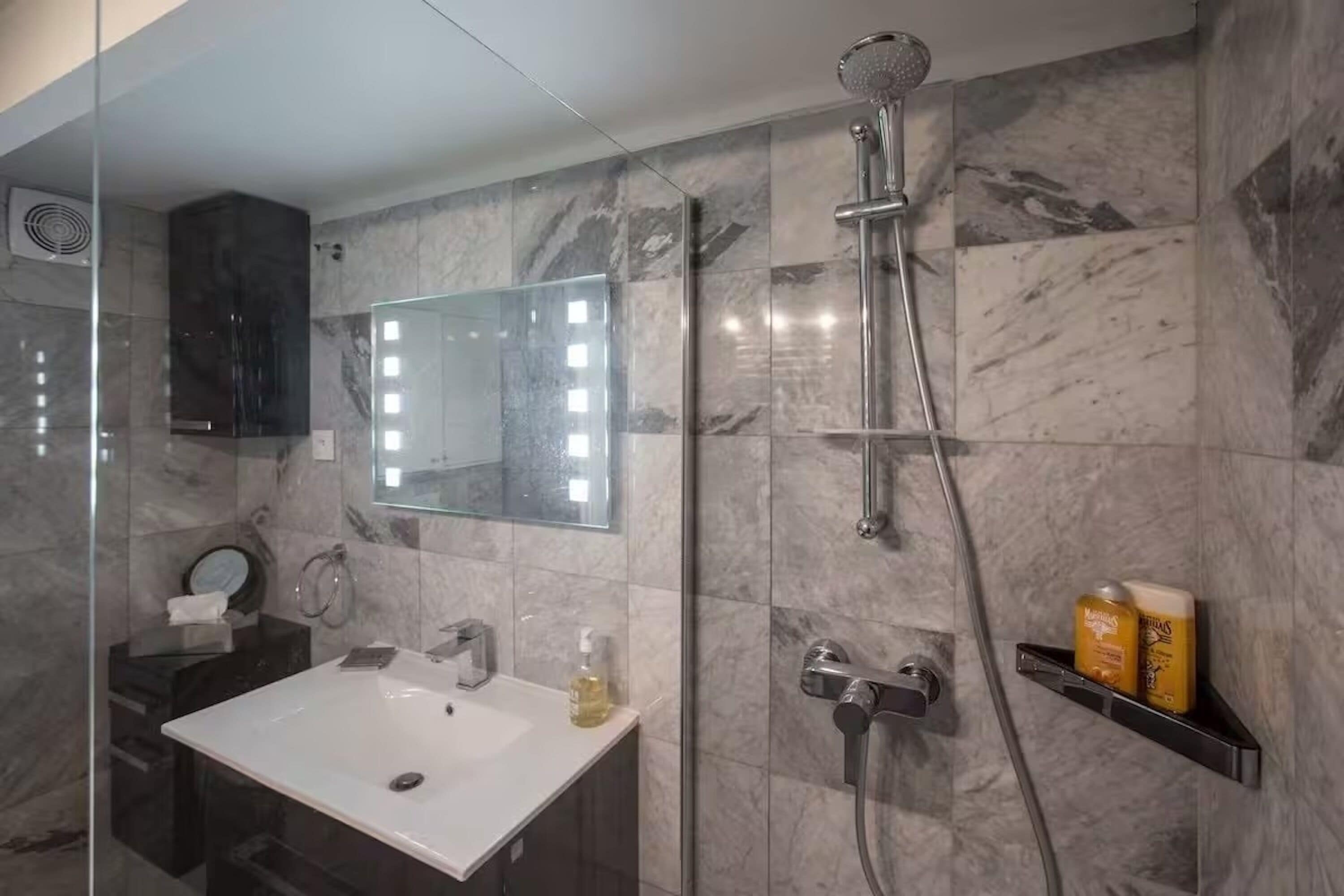 Uma casa de banho moderna com chuveiro de vidro, lavatório branco e espelho com iluminação.