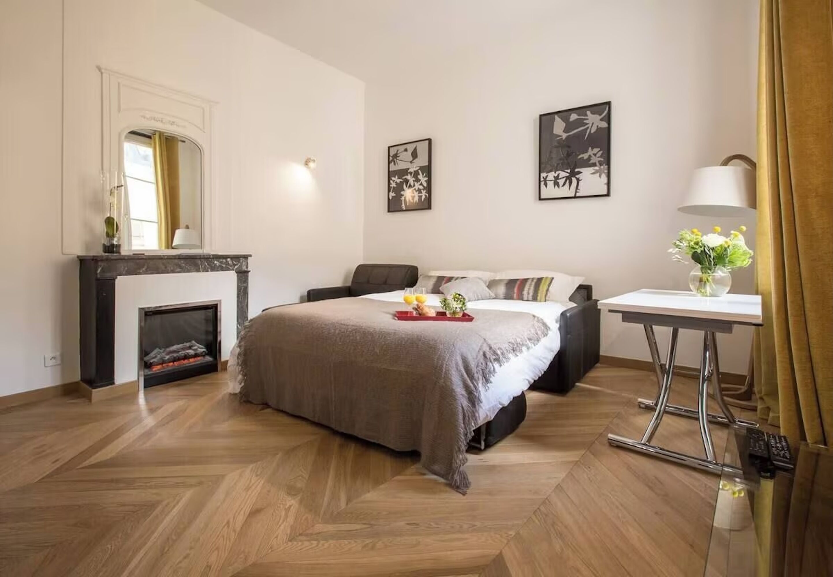 Quarto de hotel com cama, uma mesinha, lareira e obras de arte nas paredes.