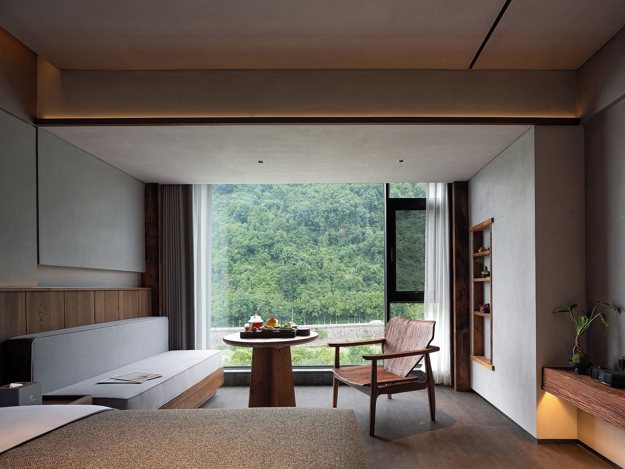 Quarto moderno com uma janela grande, uma cadeira de madeira, uma mesa redonda e um sofá.