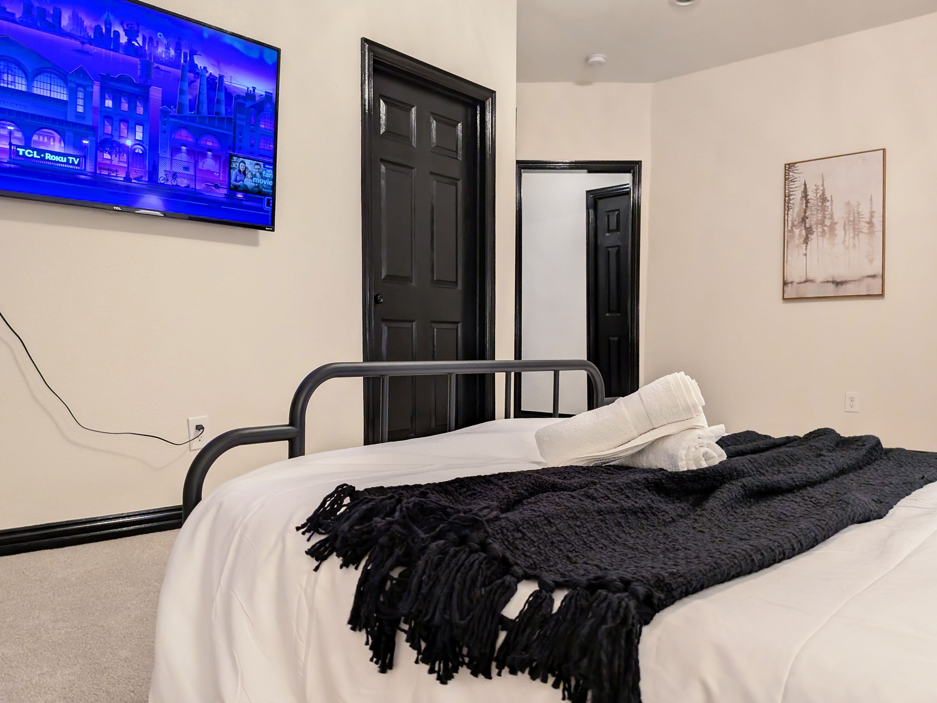 Quarto de hotel com uma cama, televisão fixada na parede, porta e um quadro na parede.