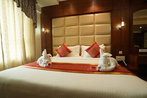 Quarto de hotel com uma cama grande, duas almofadas decorativas, um cobre-leito vermelho e dourado e duas almofadas em forma de cisne branco.