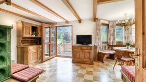 Quarto espaçoso com piso de madeira, televisão, área de jantar com mesa e cadeiras, e uma janela grande que oferece vista para o exterior.