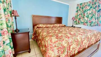 Quarto com cama de madeira, cortinas florais, mesa de cabeceira e luminária.