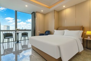 Quarto de hotel com uma cama grande, duas cadeiras, uma mesinha e vista para o horizonte da cidade.