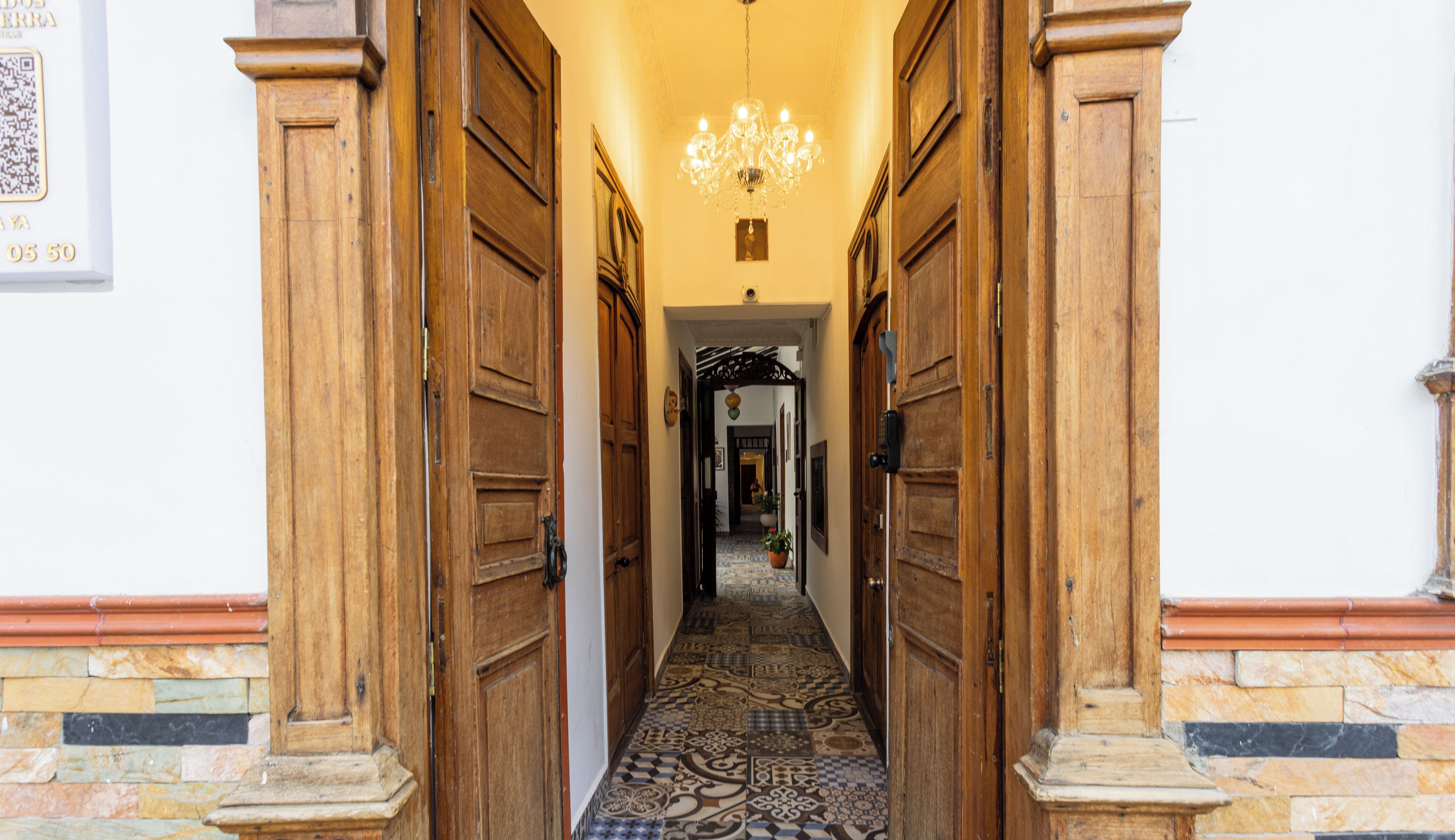 Um corredor com portas de madeira e um piso estampado, que leva a um quarto com um lustre.