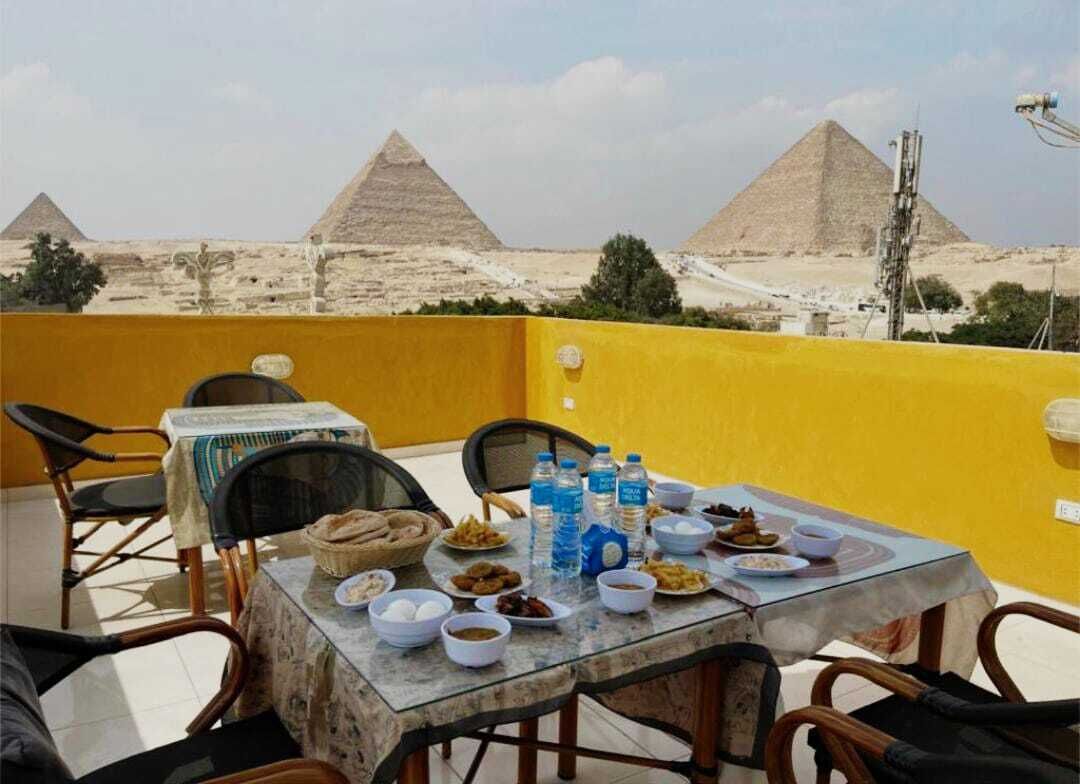 Mesa de jantar com comida e bebidas numa varanda com vista para as pirâmides.