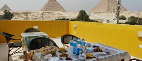 Mesa de jantar com comida e bebidas numa varanda com vista para as pirâmides.