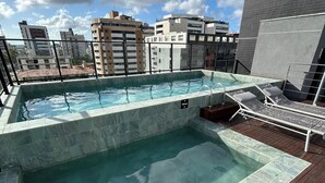 Piscina no terraço com água azul cristalina, rodeada por um deck de madeira e guarda-corpos de metal.