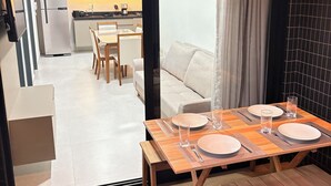 Cozinha moderna com armários brancos, geladeira de aço inoxidável e um espaço de jantar com mesa de madeira posta para quatro pessoas.