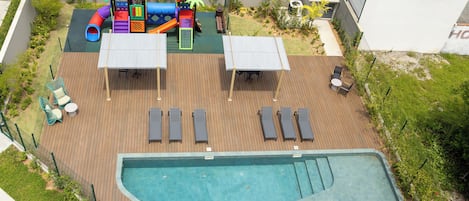 Uma área de piscina no terraço com escorrega e estrutura de recreação, cadeiras de descanso e uma pequena mesa.