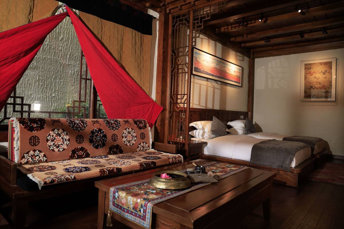 Quarto tradicional com sofá, duas camas, mesa de madeira e dossel vermelho.