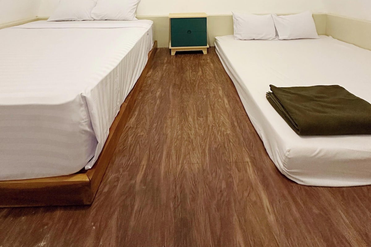 Quarto pequeno e triangular com duas camas e uma mesa de cabeceira.
