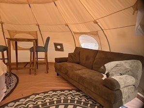 Interior de tenda com sofá, cadeiras, uma mesinha e um tapete estampado.