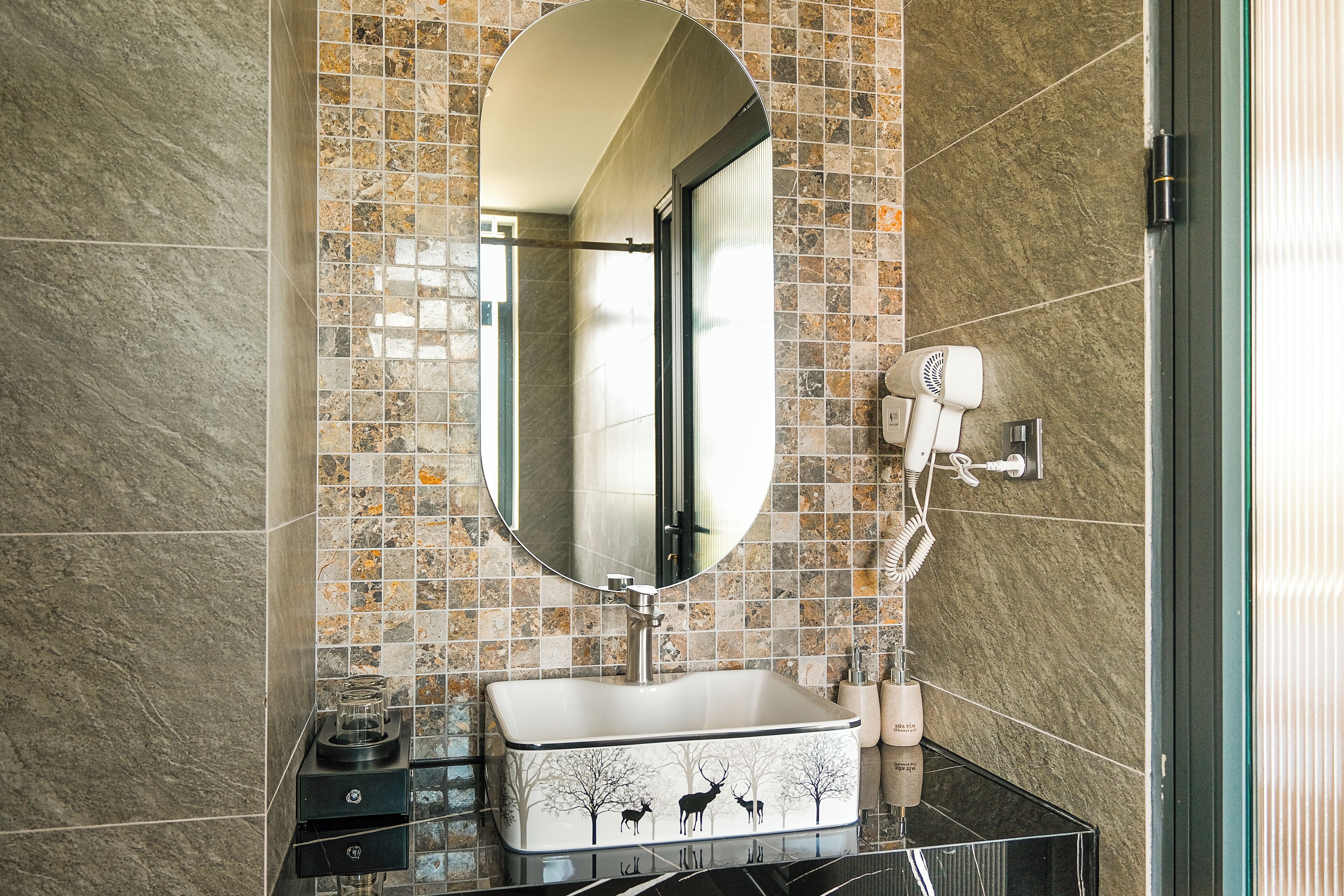 Casa de banho com painel de azulejos, espelho, lavatório e secador de cabelo fixado na parede.