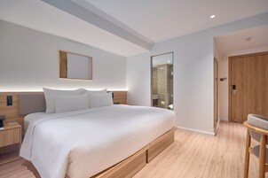 Quarto de hotel moderno com uma cama grande, mesas de cabeceira, um guarda-roupa de madeira e um pequeno espaço de estar.