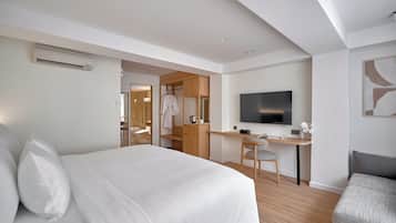 Quarto de hotel moderno com uma cama grande, escrivaninha, cadeira, televisão e guarda-roupa.