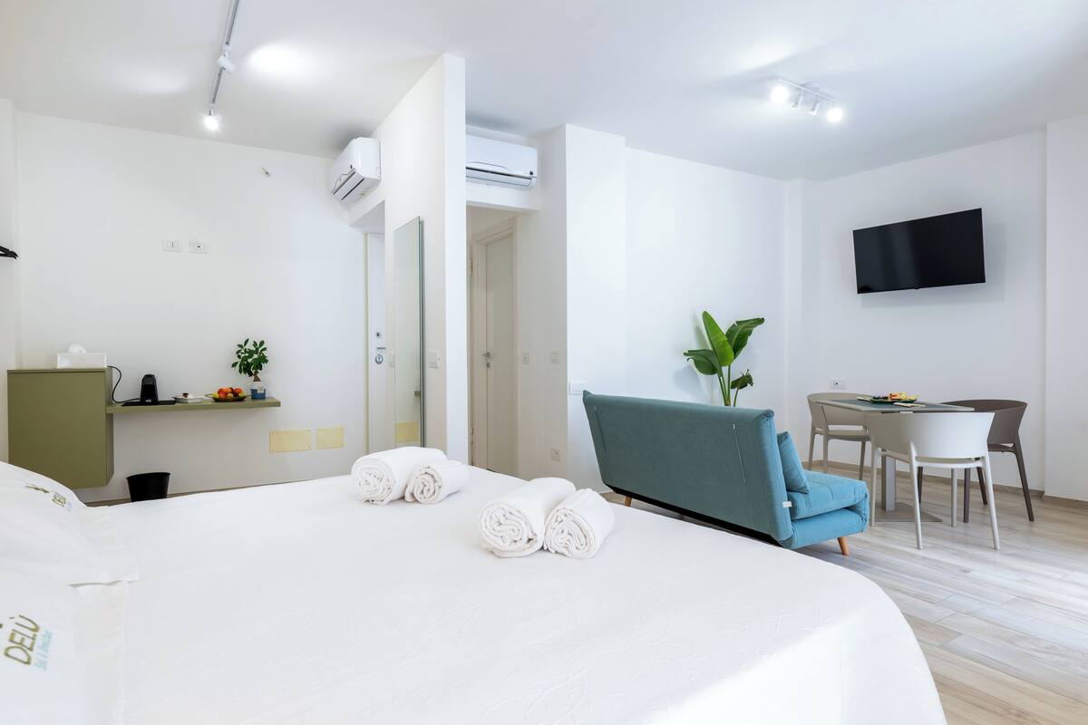 Quarto de hotel moderno com uma cama grande, uma escrivaninha, uma cadeira, uma TV e uma pequena planta.