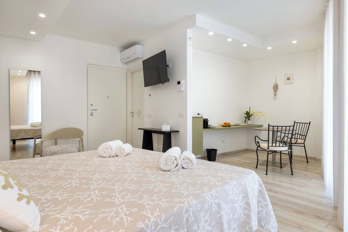 Quarto de hotel com uma cama, uma escrivaninha, uma cadeira e uma televisão fixada na parede.