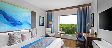 Quarto de hotel moderno com uma cama grande, uma escrivaninha, uma cadeira e uma televisão.