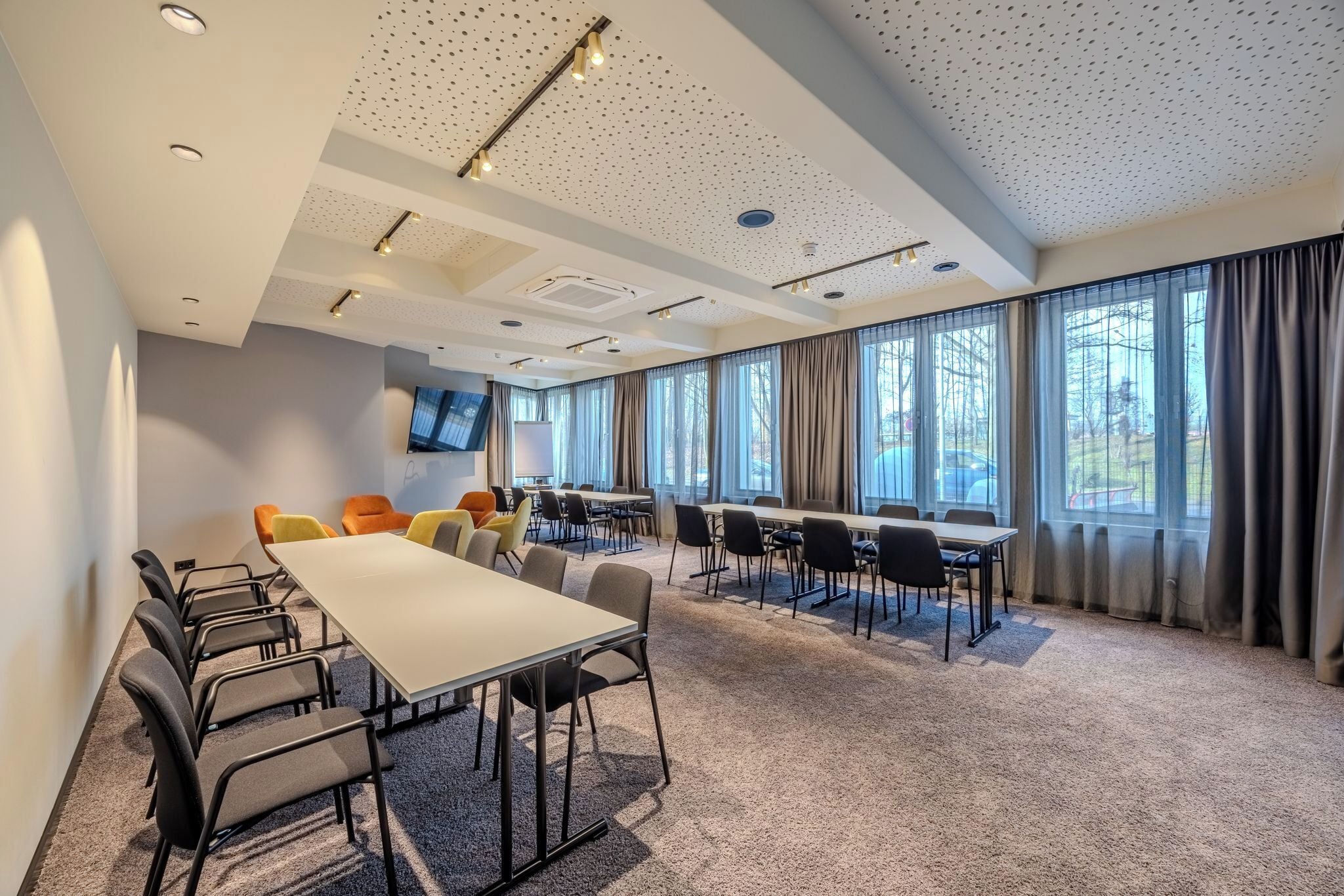 Uma sala de conferências com uma mesa comprida e cadeiras, janelas amplas com cortinas, e um design de teto moderno.