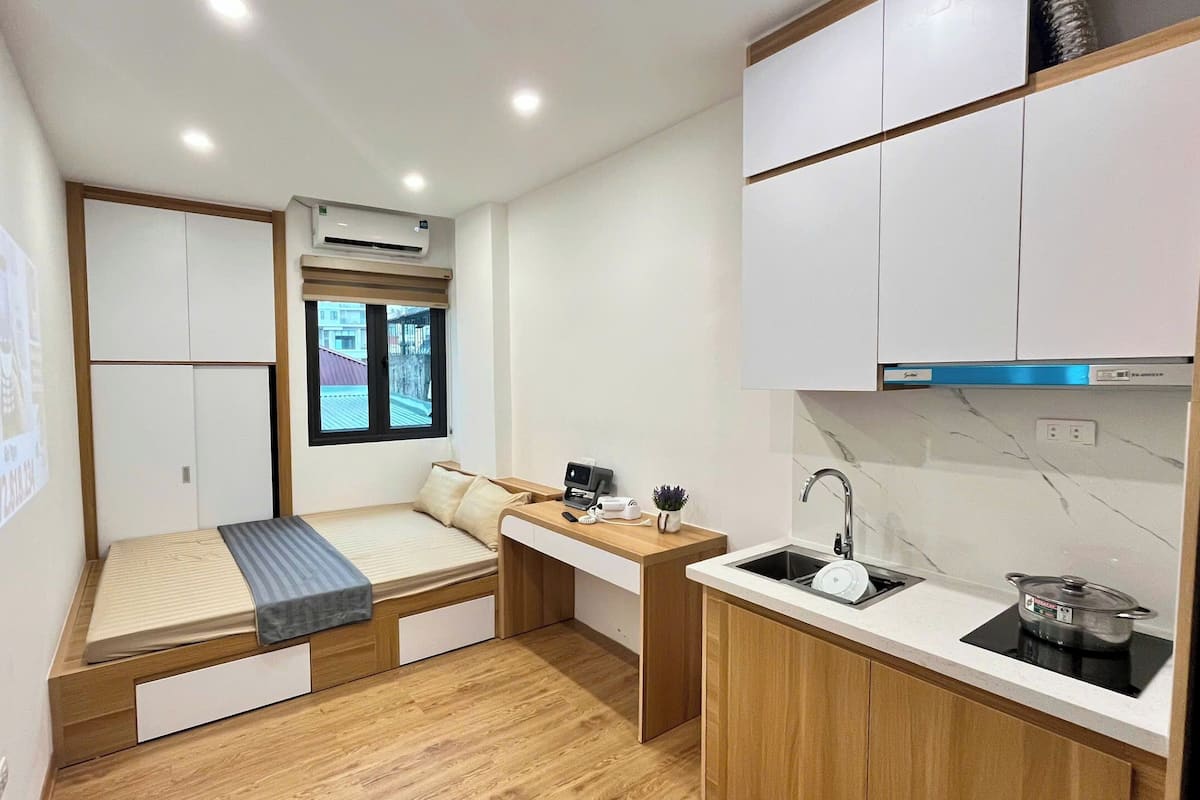 Quarto compacto com cama, pequeno espaço de cozinha, janela e guarda-roupa embutido.