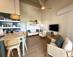 Uma sala de estar moderna com um sofá, cadeiras, uma mesa de jantar, uma televisão e um ventilador de teto.