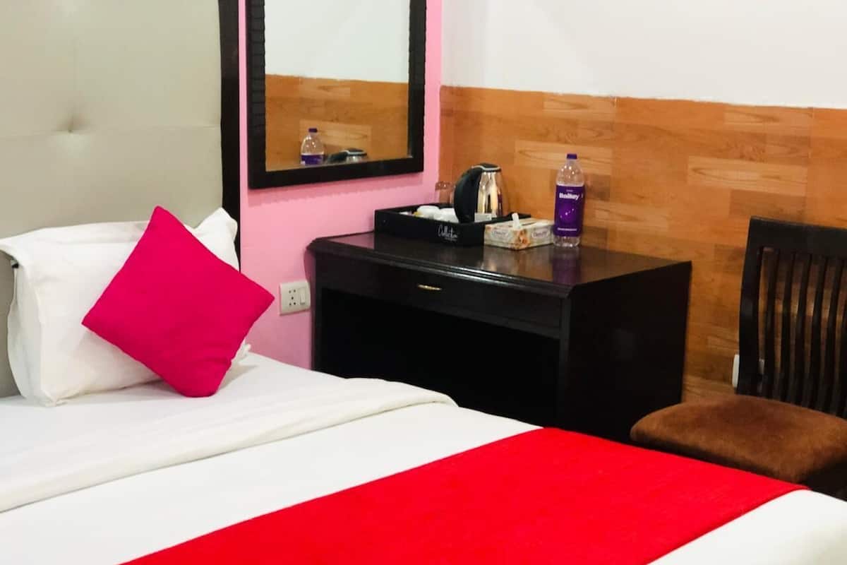 Quarto de hotel com cama, escrivaninha preta, cadeira e espelho.