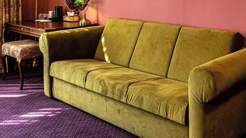 Um sofá verde em um quarto com carpete roxo, uma escrivaninha de madeira, uma luminária e um espelho.