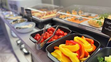 Buffet com diversas opções de comida, incluindo tomates, pimentões e um aviso indicando sanduíches de cream cheese e pepino.