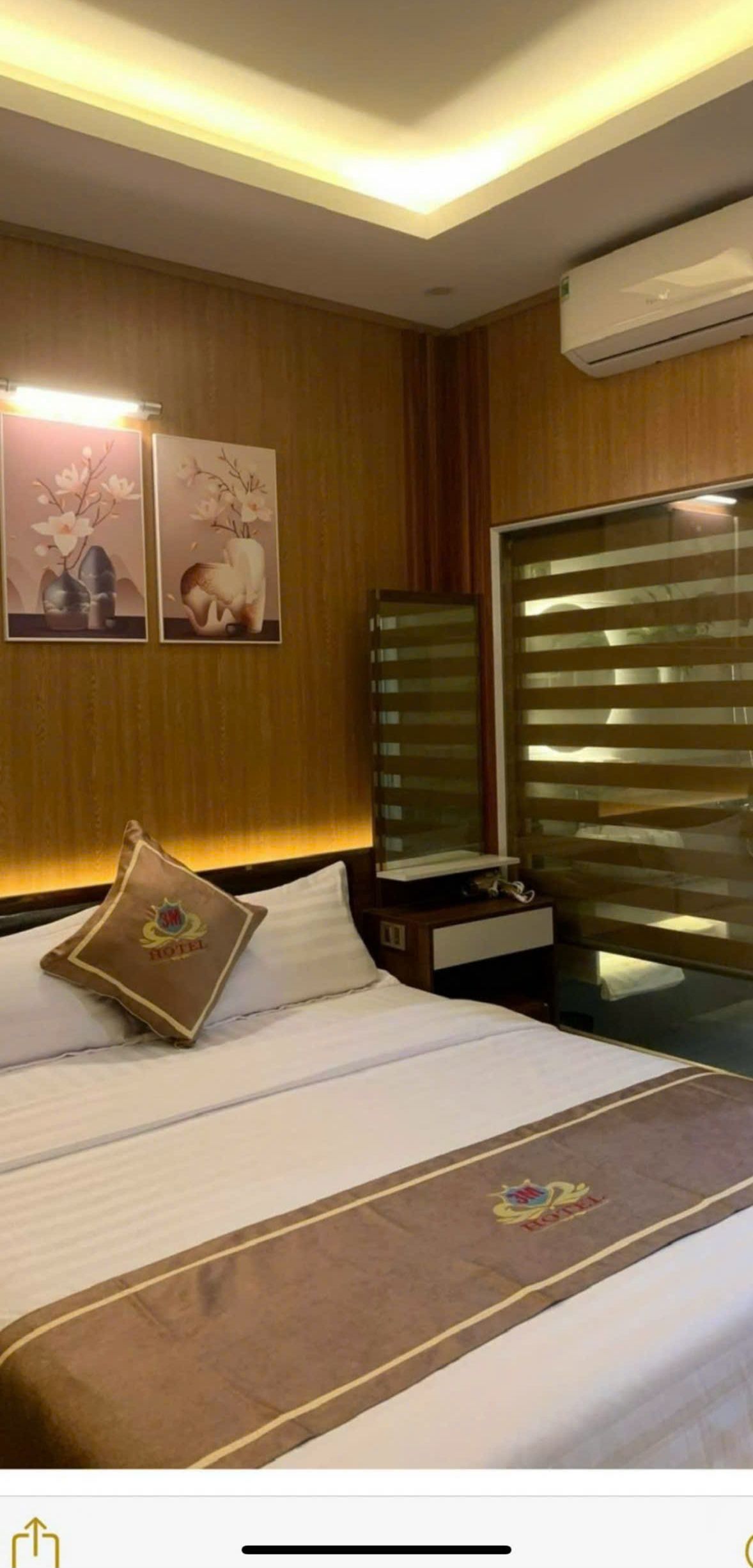 Quarto de hotel com cama, mesa de cabeceira, espelho e janela com persianas.