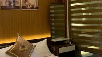 Quarto de hotel com cama, mesa de cabeceira, espelho e janela com persianas.