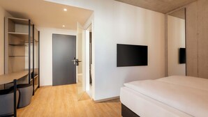 Quarto moderno com cama, televisão na parede, secretária com cadeira e guarda-roupa.