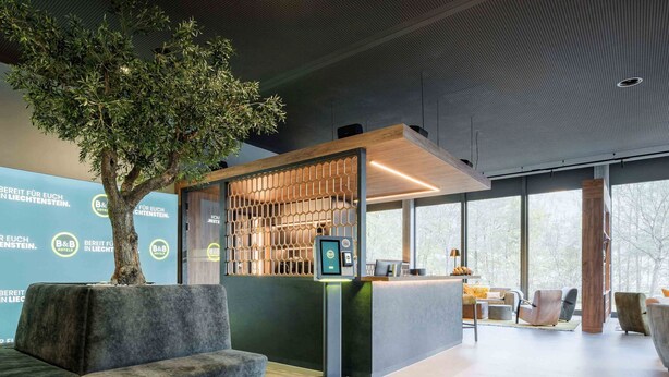 Uma área de recepção moderna, com balcão, espaço para sentar e uma grande janela com vista para árvores.