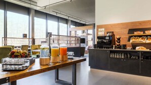 Um café moderno com uma mesa de madeira comprida, dispensadores de suco e uma estação de café.