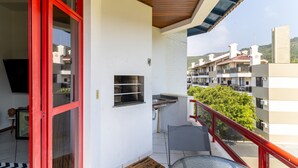 Uma varanda com guarda-corpo vermelho, uma pequena cozinha externa e vista para edifícios vizinhos.
