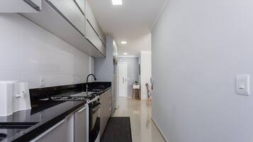 Cozinha moderna com armários brancos, bancada preta e eletrodomésticos de aço inoxidável.