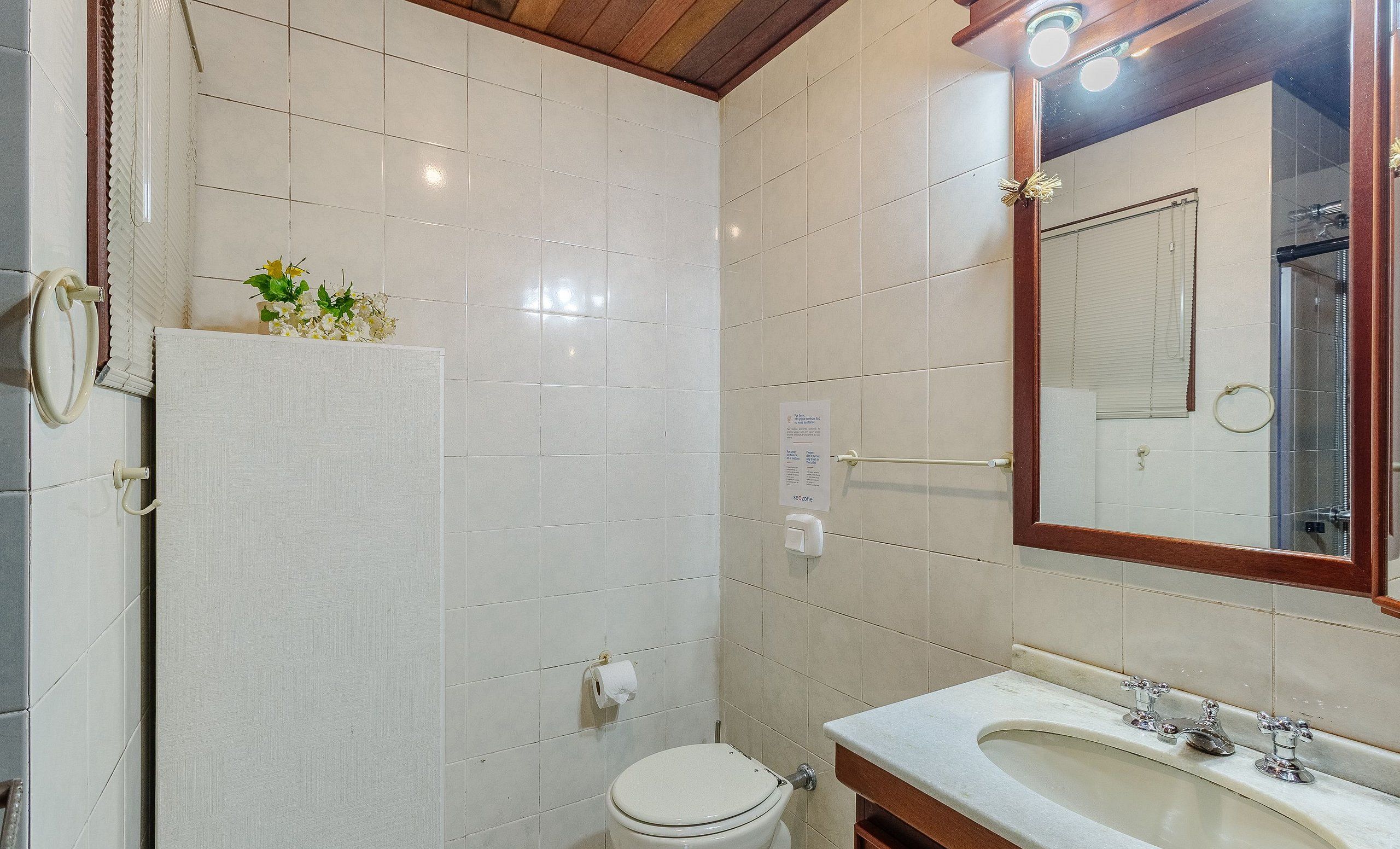 Casa de banho com azulejos brancos, sanita, lavatório com espelho e um porta-toalhas.