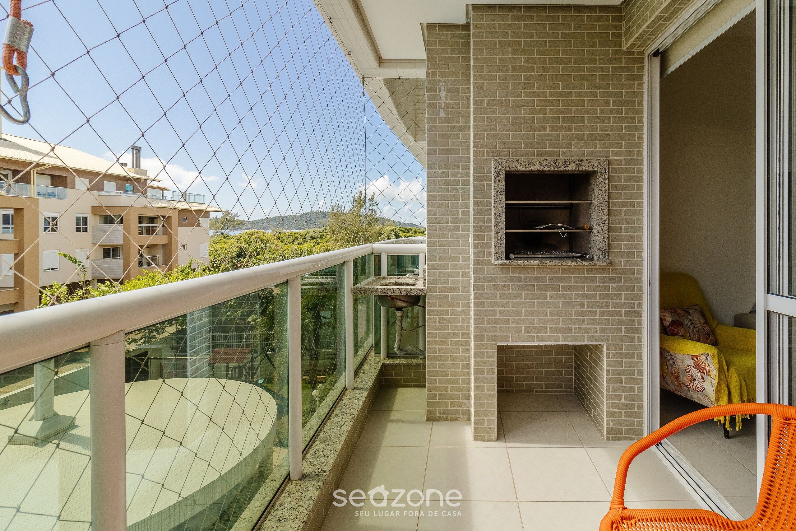 Uma varanda com guarda-corpo de vidro, lareira de tijolos e vista para um edifício ao fundo.