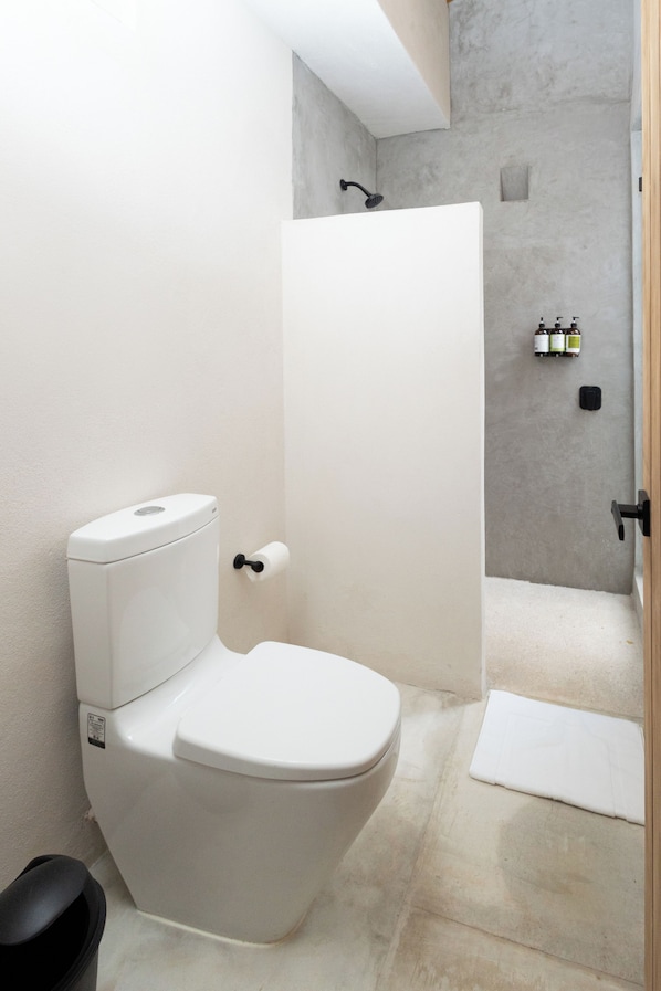 Uma casa de banho moderna com sanita, chuveiro e um tapete pequeno no chão.