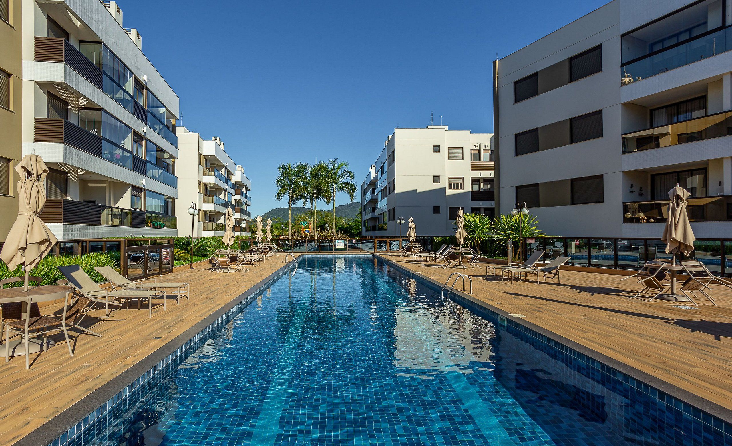 Piscina com espreguiçadeiras e guarda-sóis, cercada por edifícios de apartamentos modernos.
