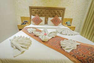 Cama bem arrumada com toalhas dispostas em um padrão decorativo, cabeceira estofada e colcha estampada.